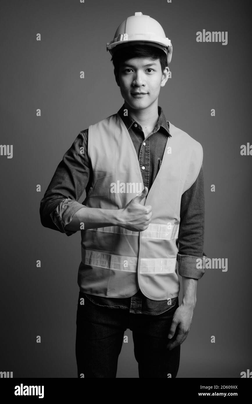 Young handsome Asian man construction worker against gray background ...