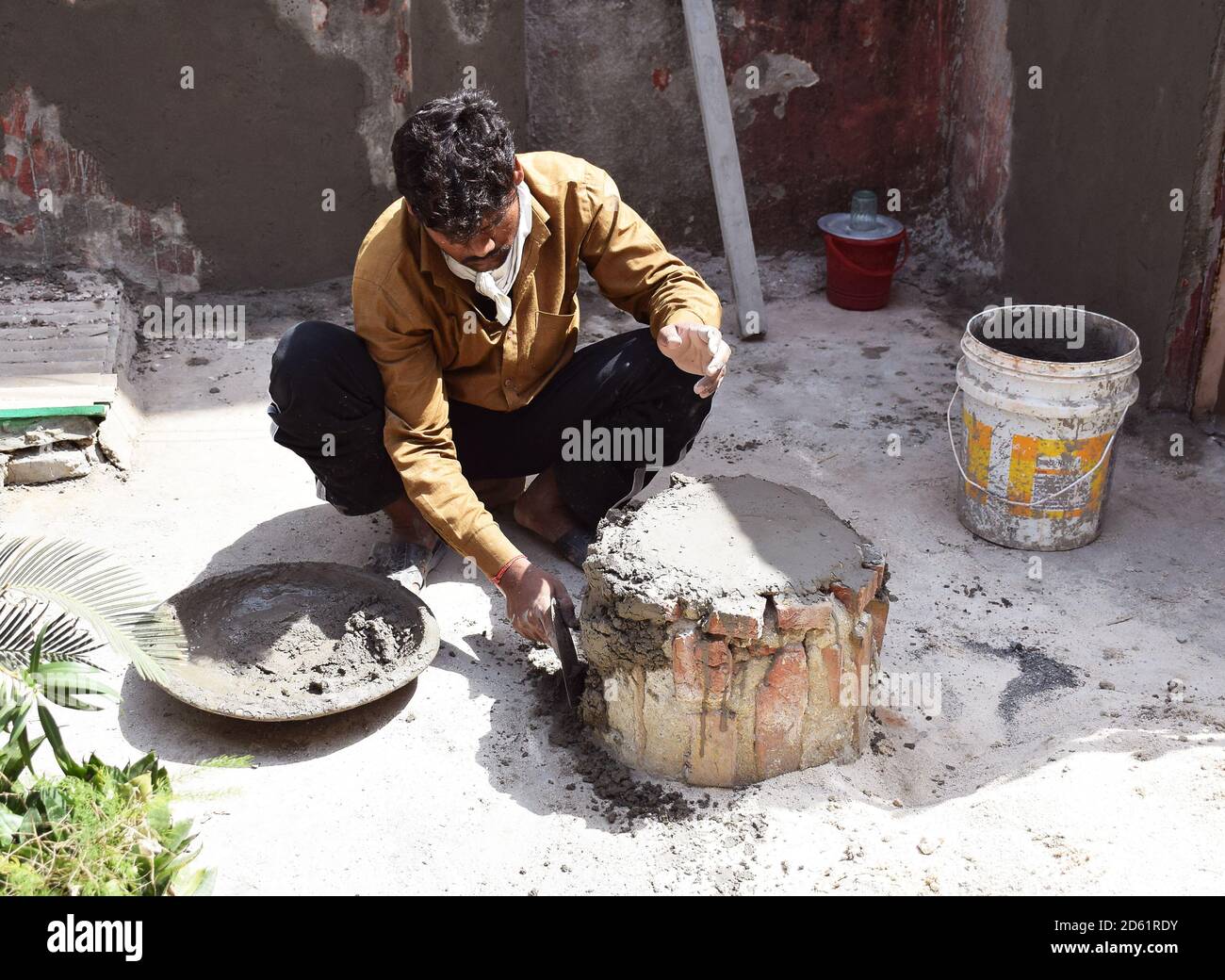 An Indian labour or construction worker plastering a pillar with cement ...