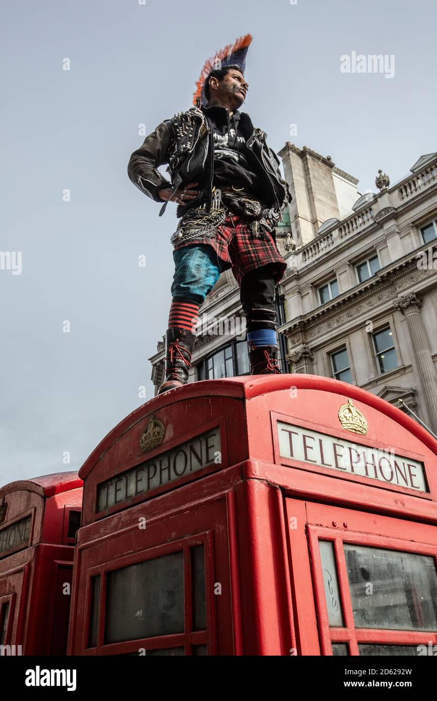 Punk rocker with mohican hair sits relaxing on top of red telephone ...