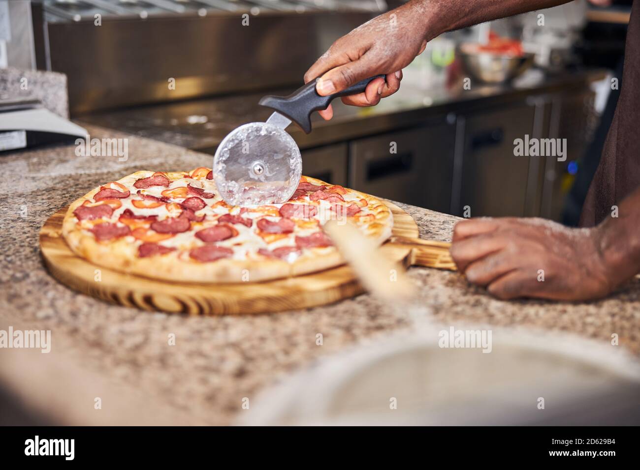 Male hand cutting pepperoni pizza in pizzeria Stock Photo - Alamy