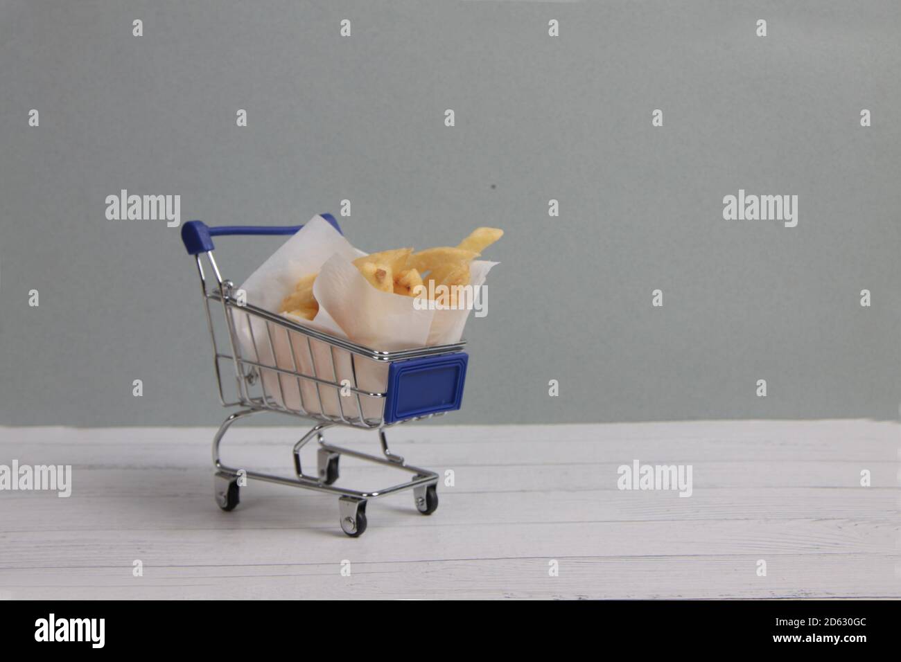 shopping cart of french fries on wooden table against gray background ...