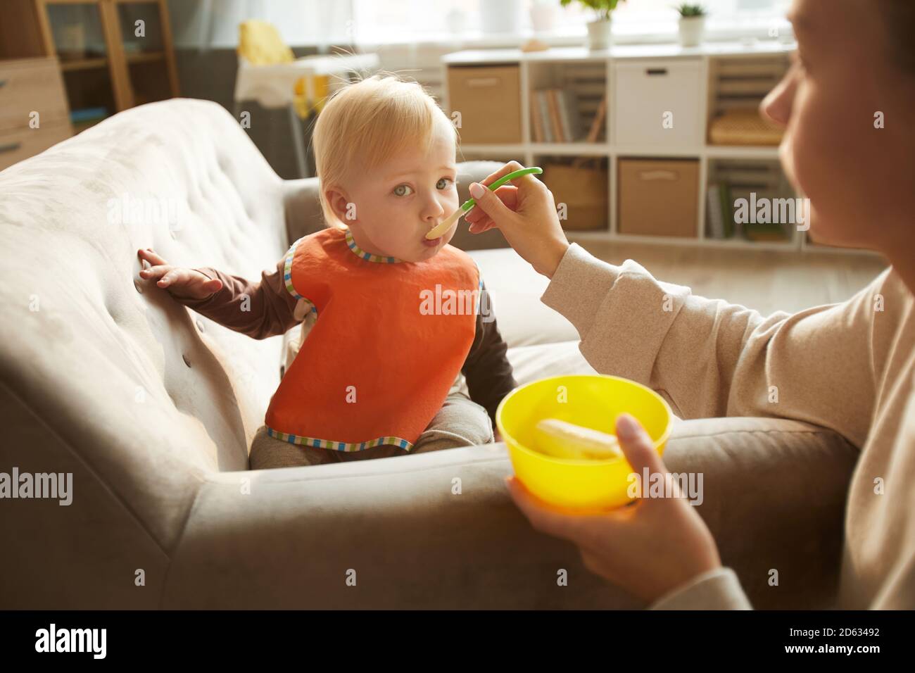 Baby boy eating with the help of his mother during lunch time at home ...