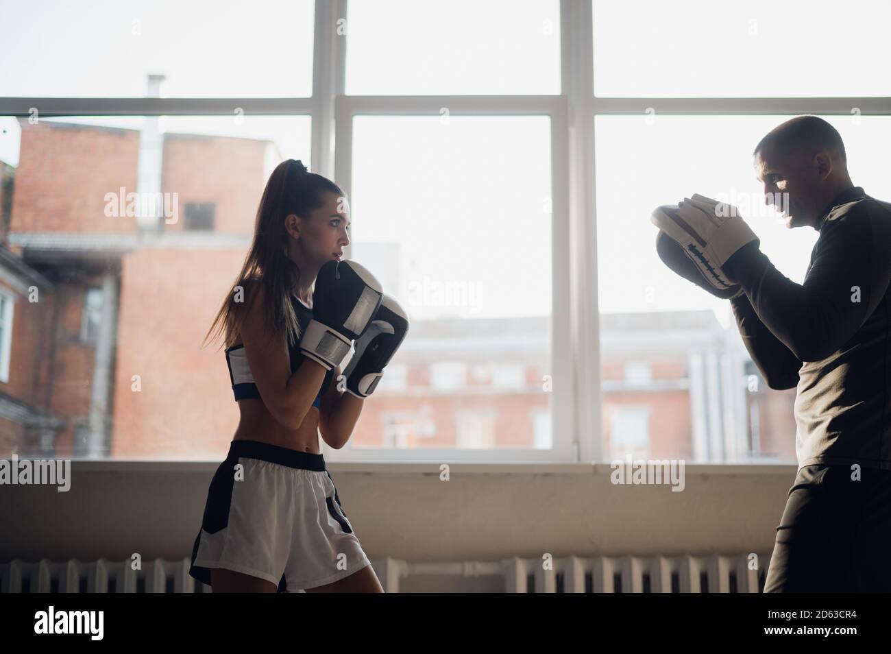 A young girl conducts kickboxing training and practices paw strikes ...