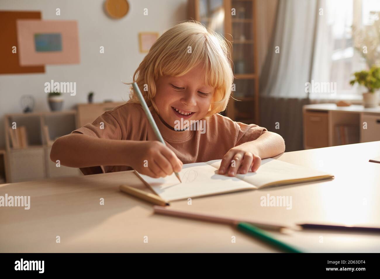Little boy sitting at the table and making notes in notebook he doing ...