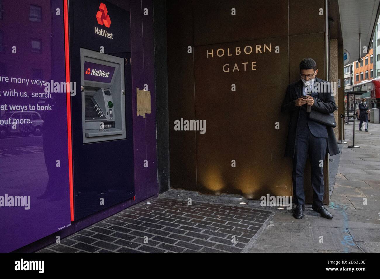 Business man on his phone wearing his facemask around his chin whilst stood at Holborn Gate ...