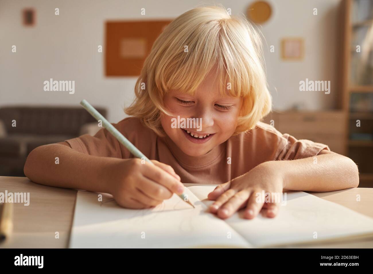 Child with blond hair writing the report in note book he doing homework ...