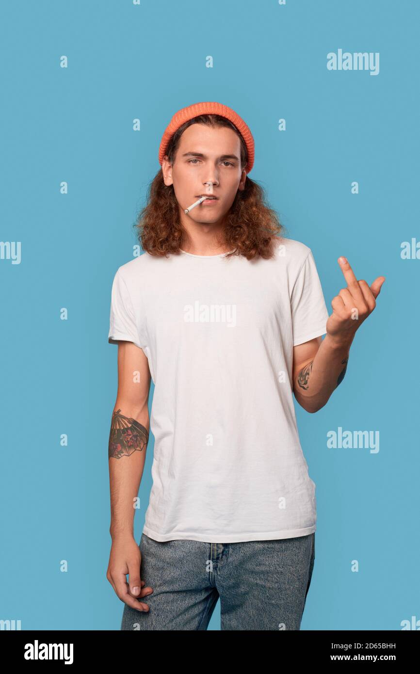 Freestyle. Curly-haired guy wearing hat standing isolated on blue ...