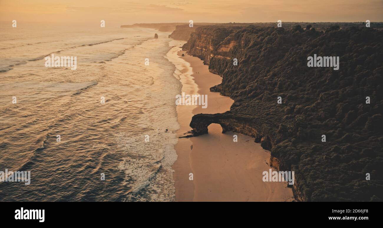 Sunset ocean seascape with waves at rock wall on sand beach aerial view ...
