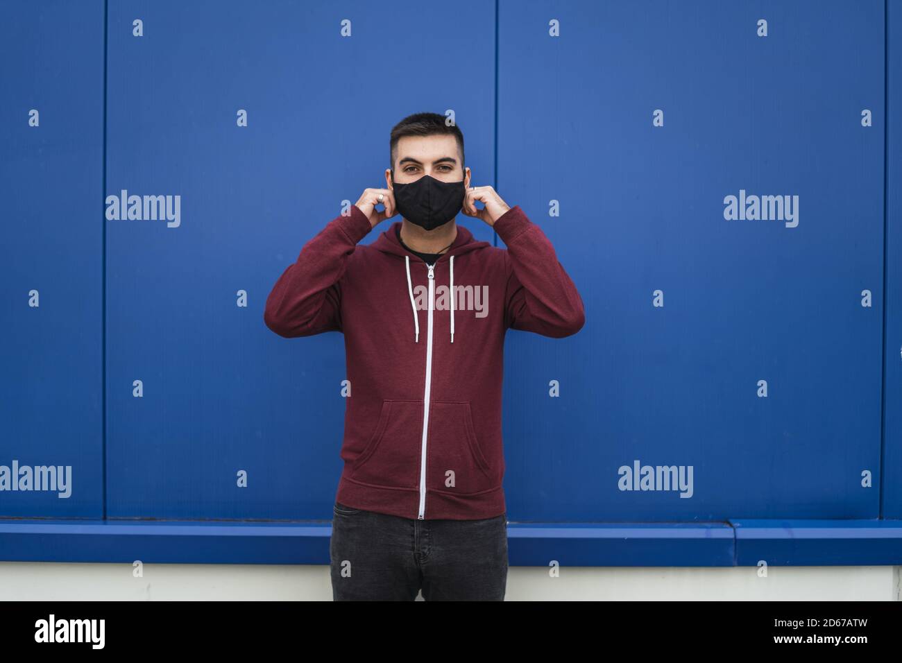 Male model wearing a face mask while standing by a blue wall Stock ...