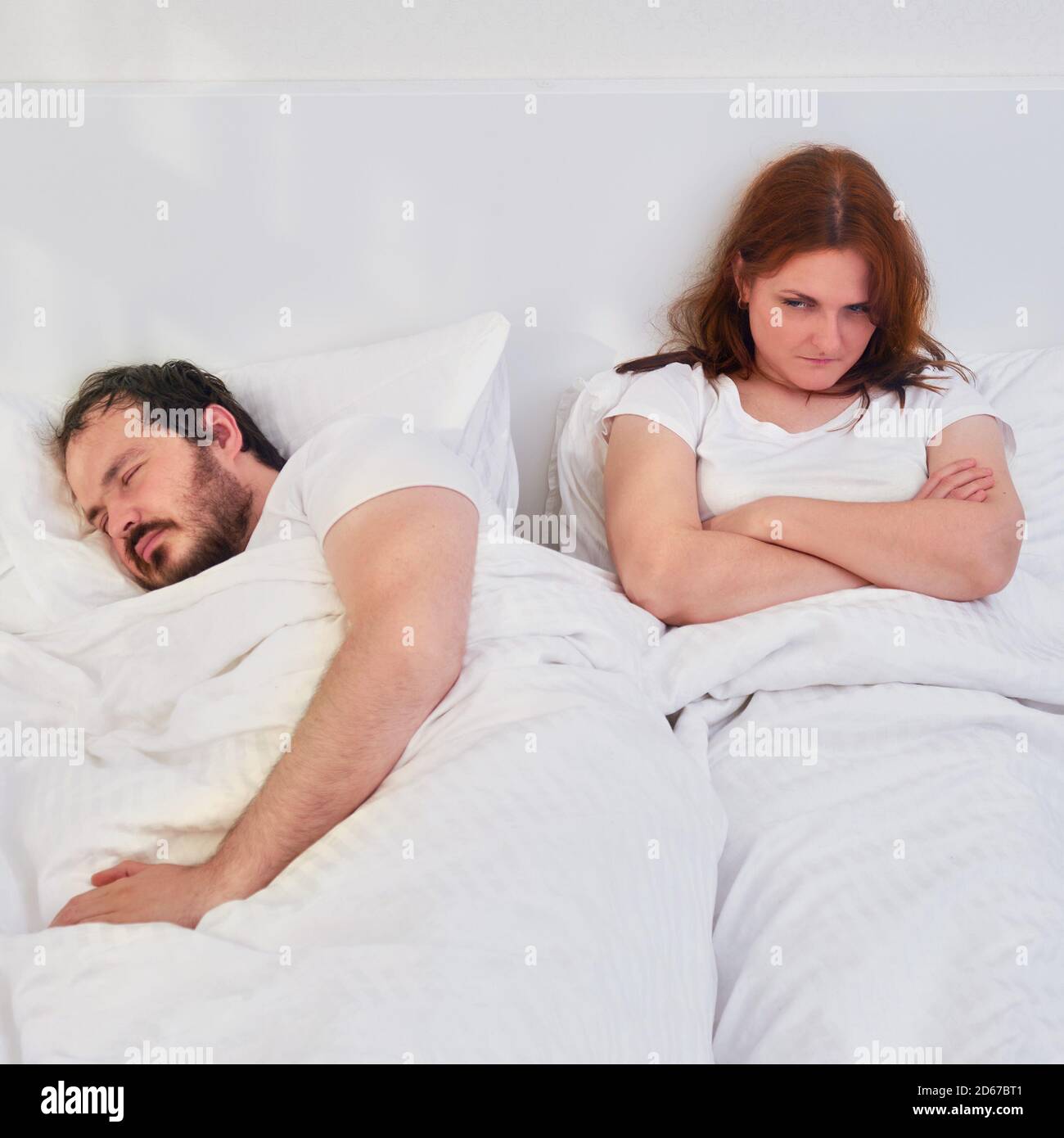 Unhappy a woman lying next to man sleeping in white bed, concept ...