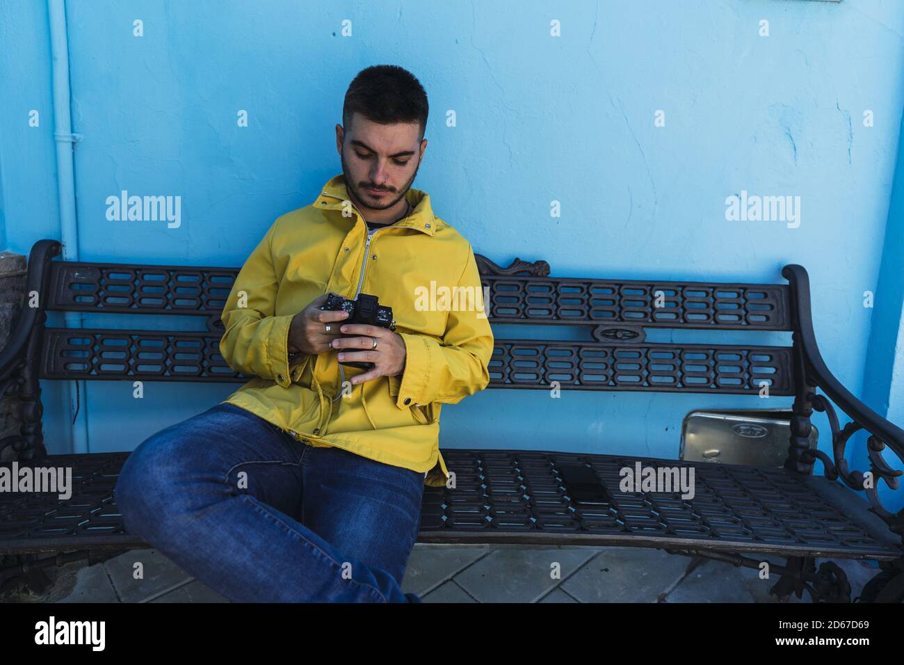 Male using his camera while sitting by a blue wall Stock Photo - Alamy