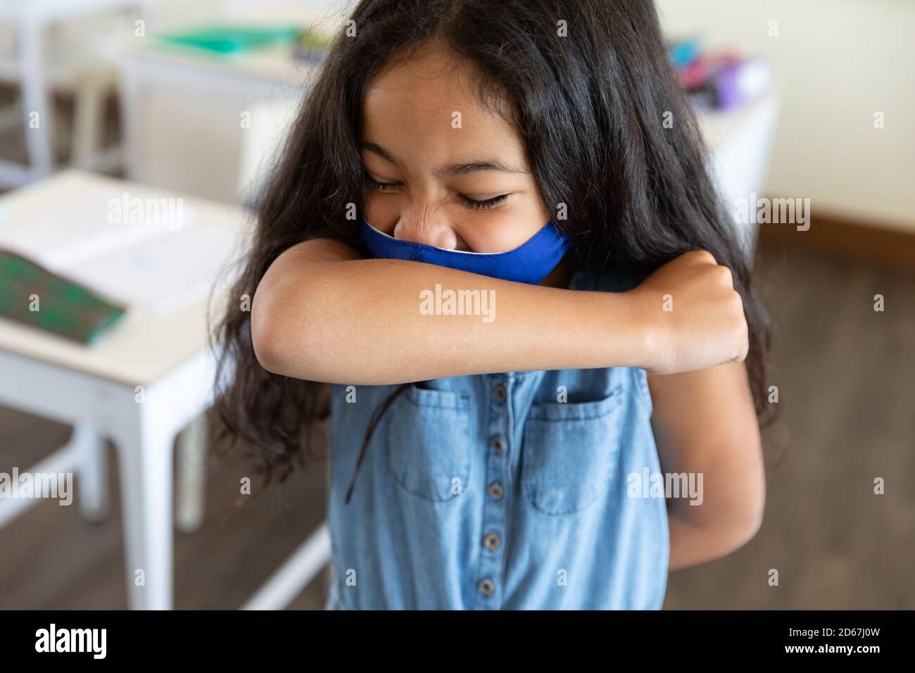 Girl wearing face mask sneezing while covering her mouth at school ...