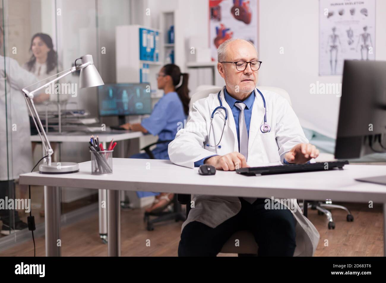 Elderly aged doctor using computer in hospital cabinet while young ...