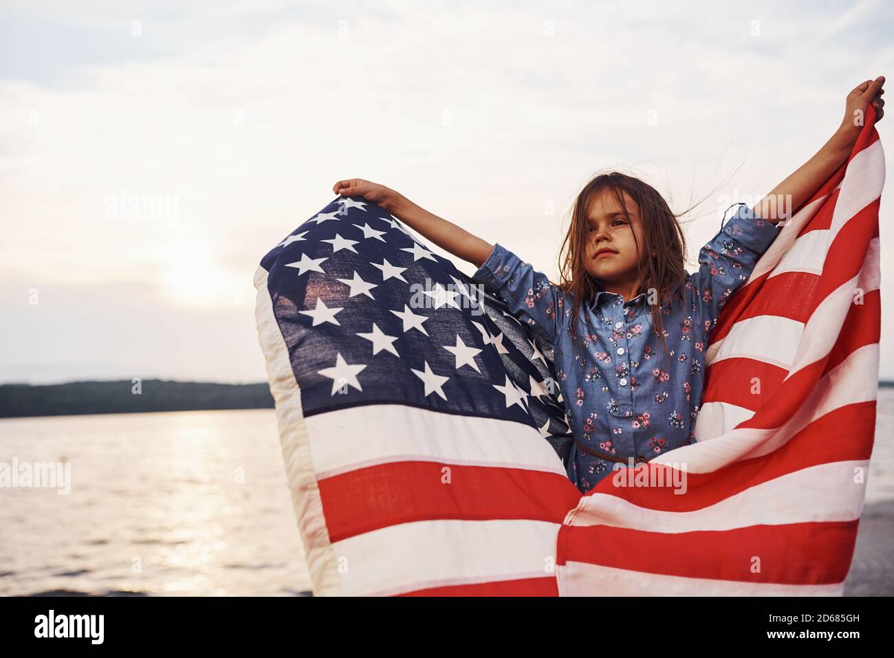 Patriotic female kid with American Flag in hands. Against cloudy sky ...