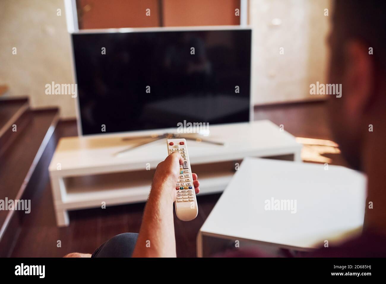 Backing view of man holds remote controller in hand and turning on TV ...