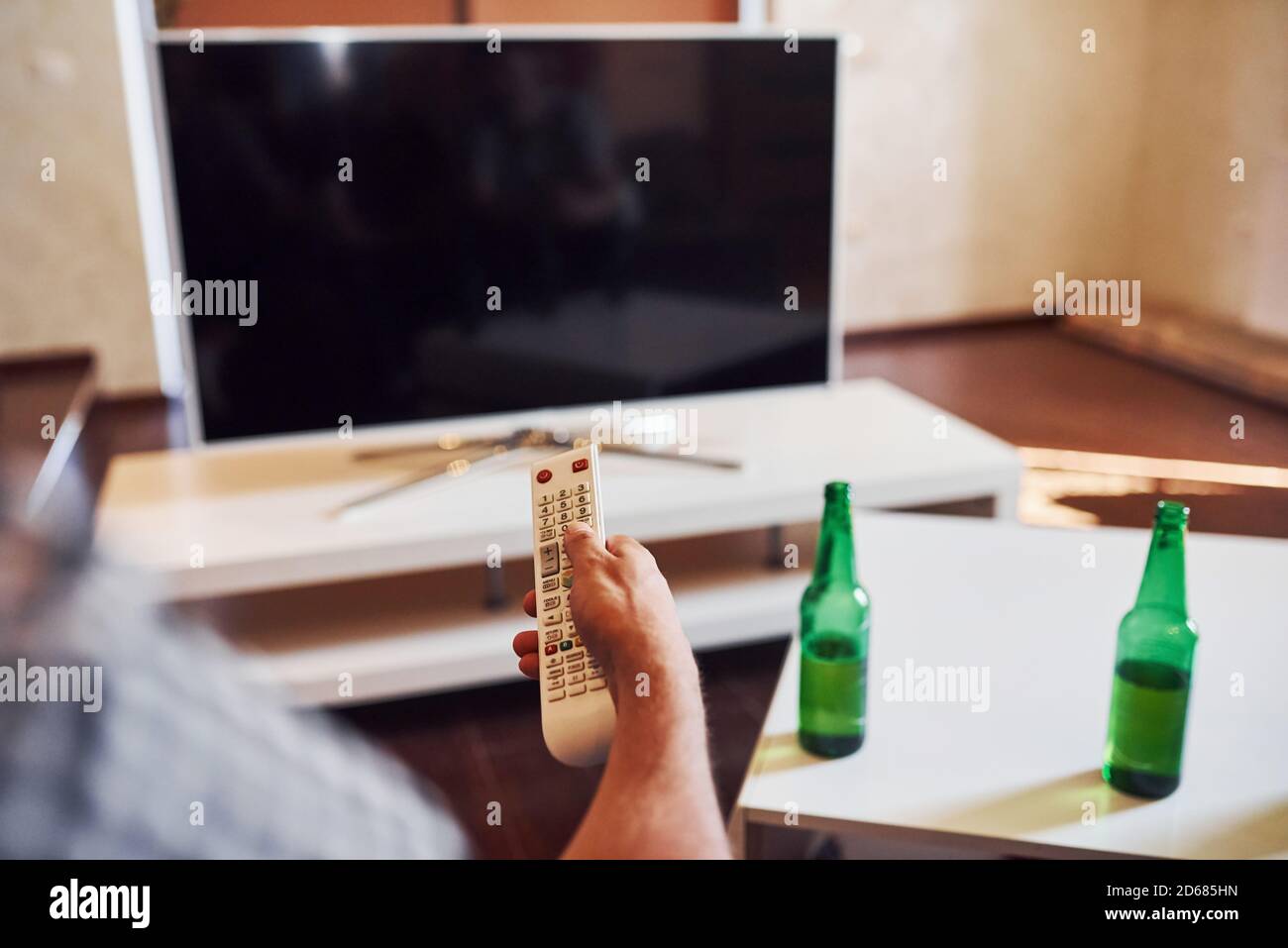 With beer on table. Backing view of man holds remote controller in hand ...