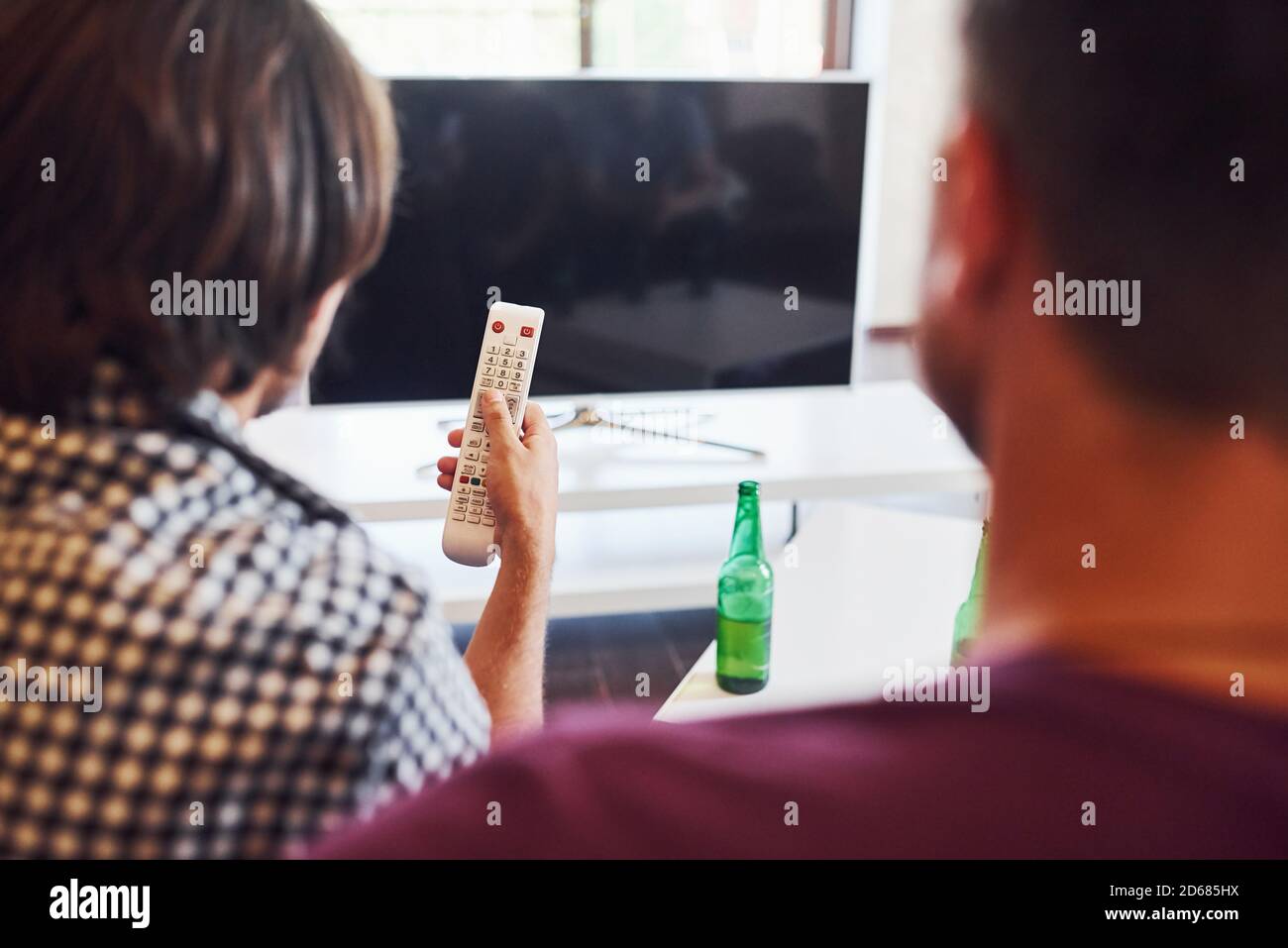 Rear view of friends watching TV and holds remote controller in hand ...