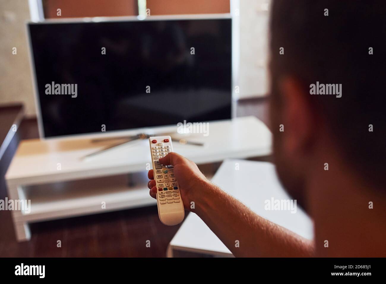Backing view of man holds remote controller in hand and turning on TV ...