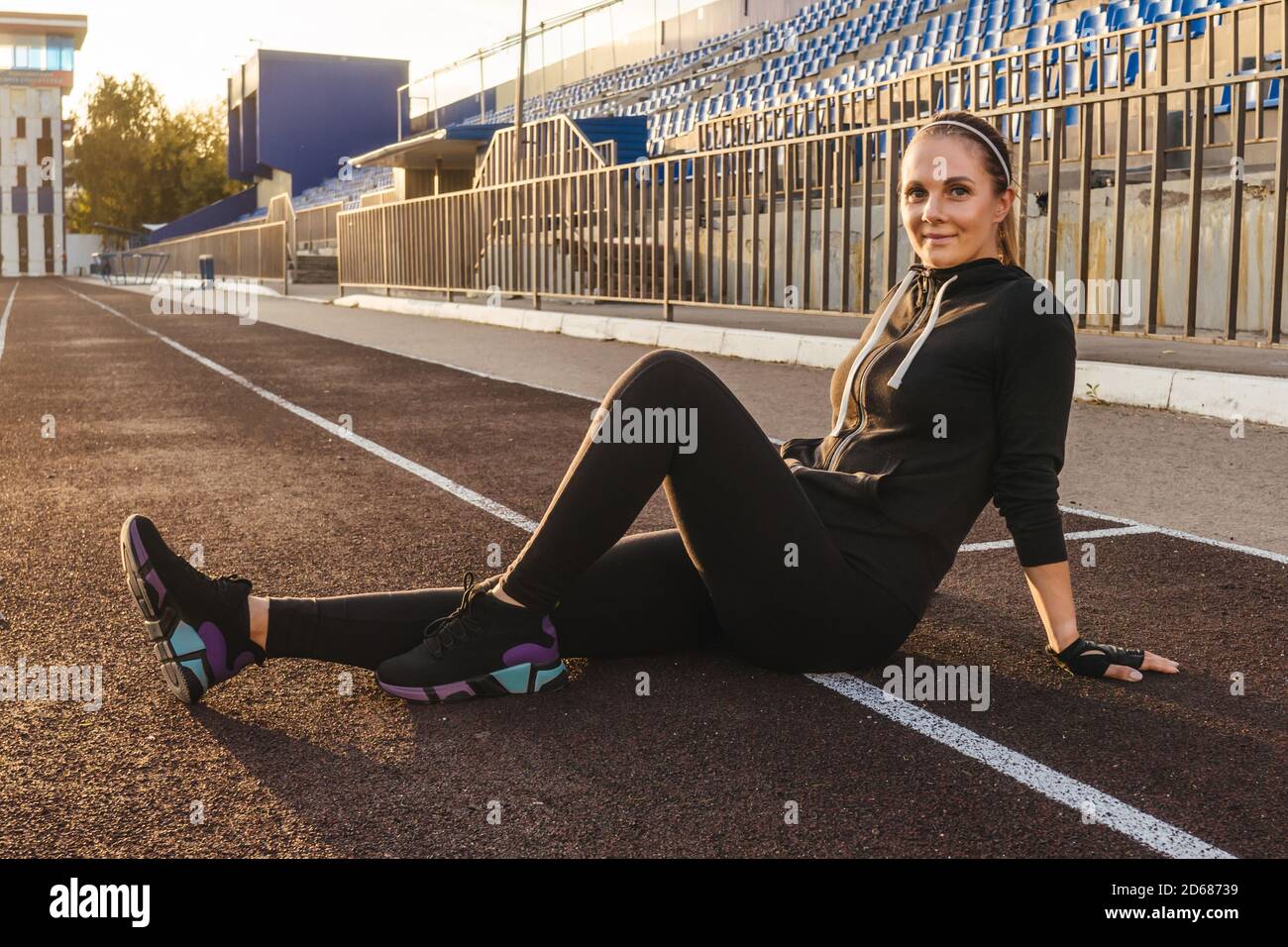 Fitness woman in black tracksuit sitting on stadium track. Woman after ...