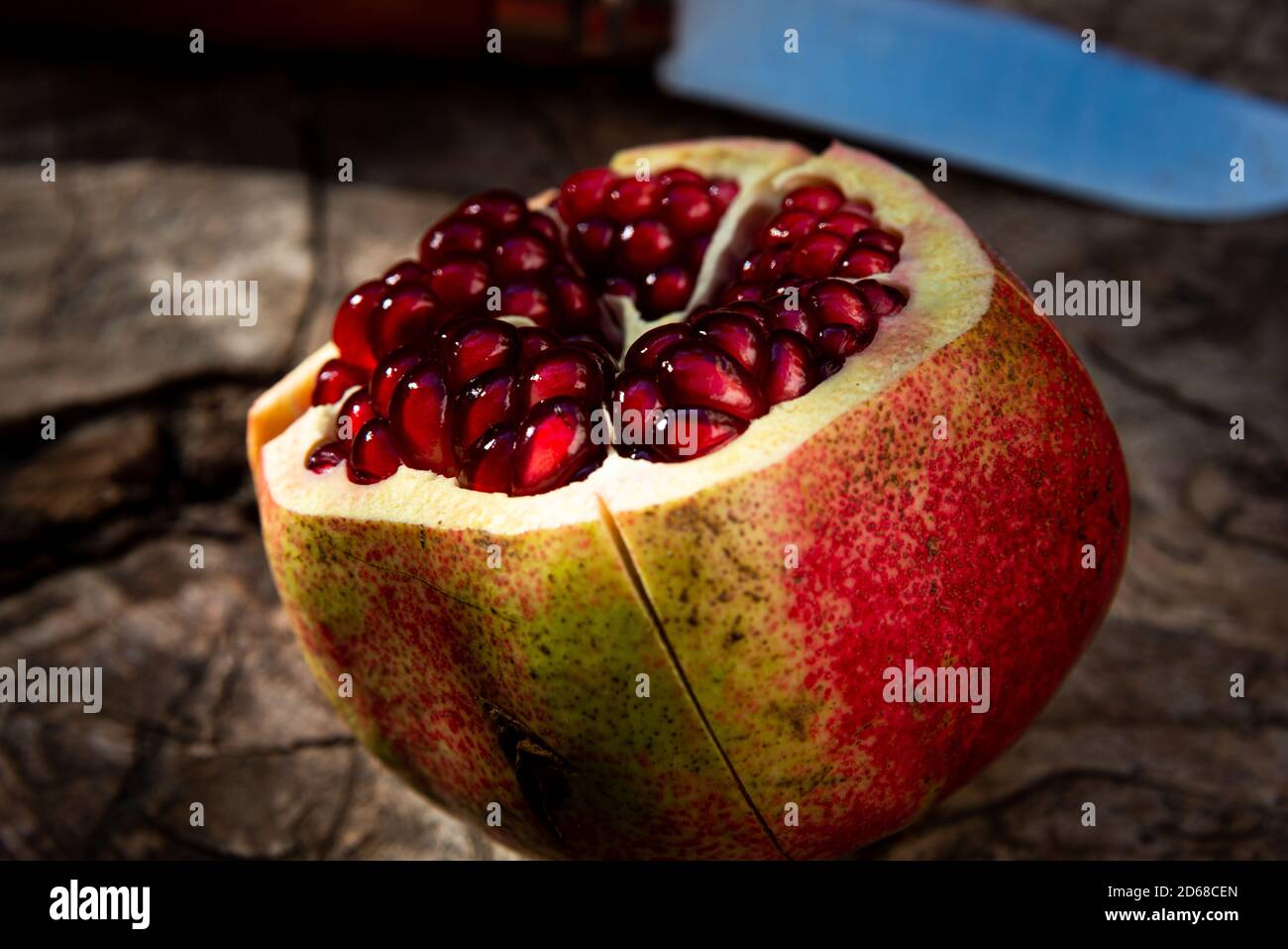 Cut open Pomegranate showing colouful seeds on rustic wooden table with ...