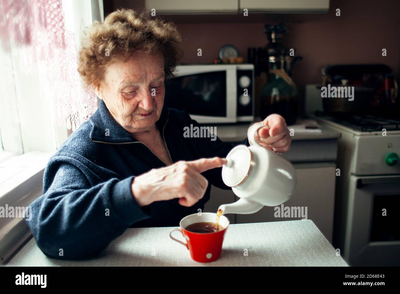 An old woman drinking tea in the kitchen Stock Photo - Alamy