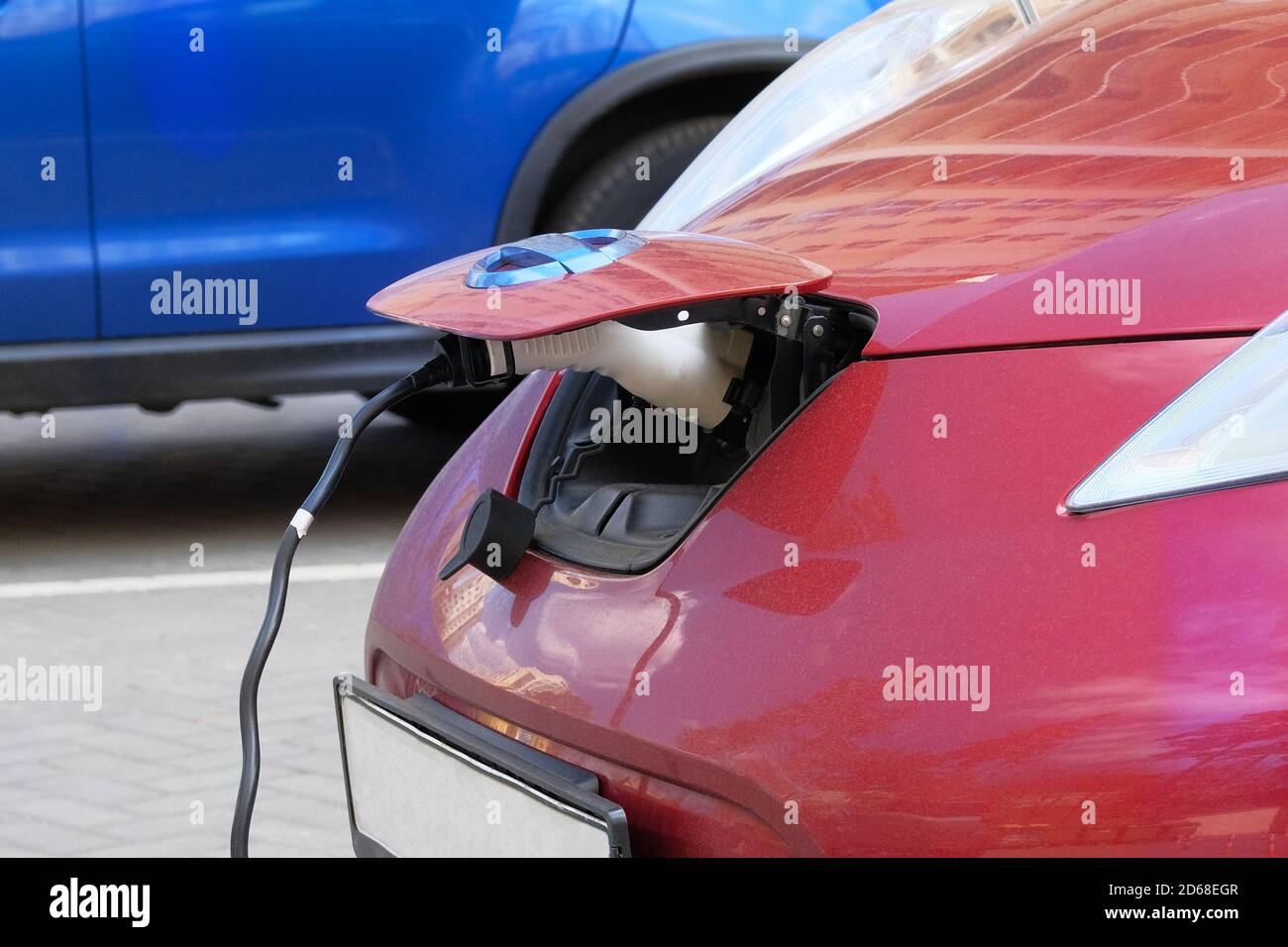 Red car is charged on electric charging station in parking lot. Close ...