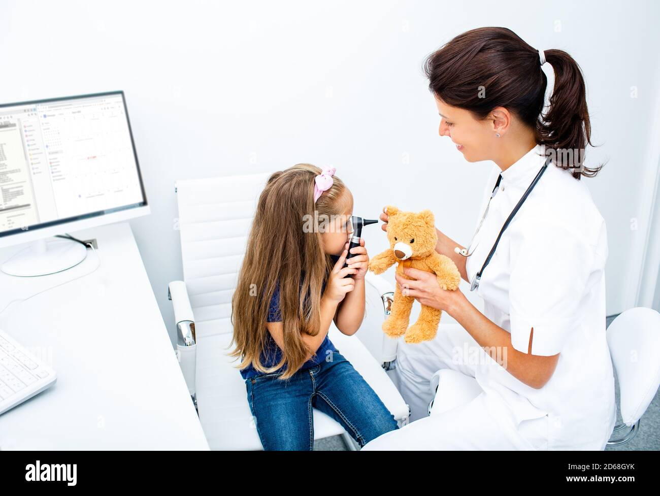 little girl looking through the otoscope on the toy's ear. Pediatrician ...