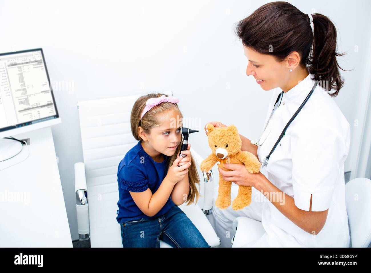 little girl looking through the otoscope on the toy's ear. Audiologist ...