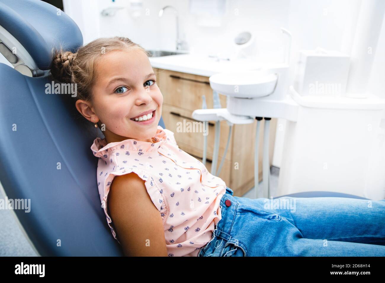 Pretty child with a perfect healthy smile, sitting in the dentist's ...