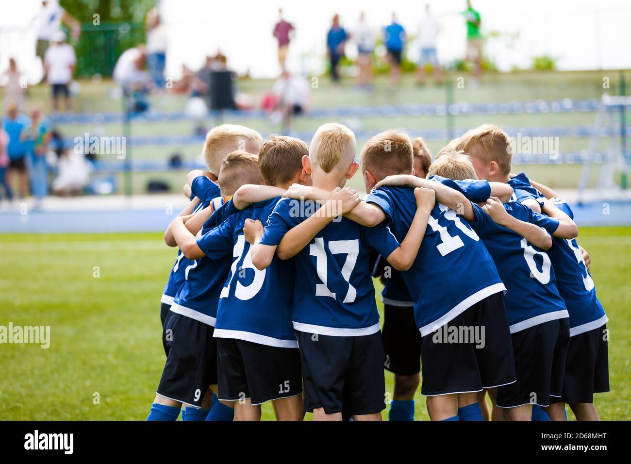 Boys football team forming huddle. Happy kids in a sports team on grass pitch. Summer school ...