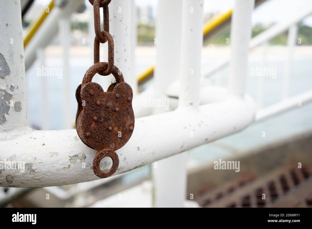 A brown rusty metallic lock hangs on a rusty white lattice of a river ...