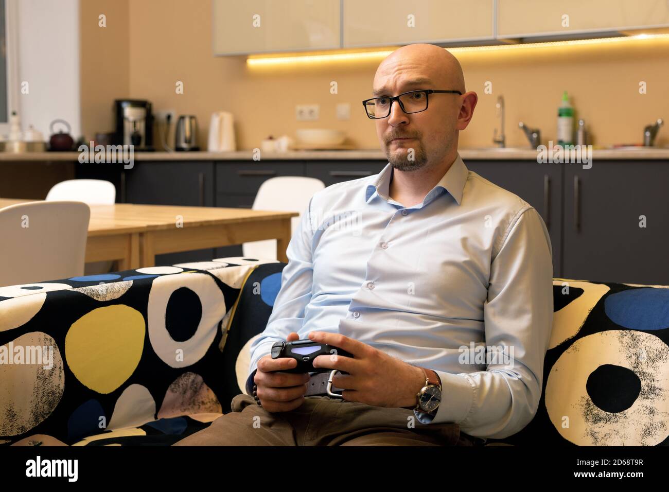 middle-aged bald man with glasses is playing video games with joystick ...