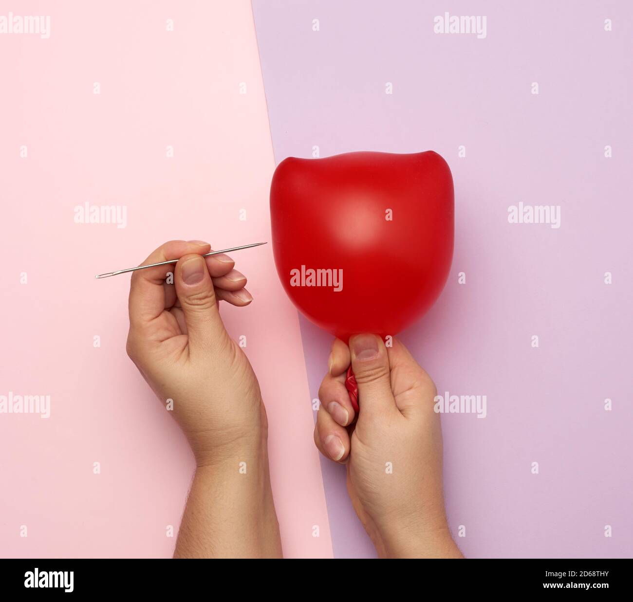 female hand holding a red balloon and a sharp metal needle on a pink ...