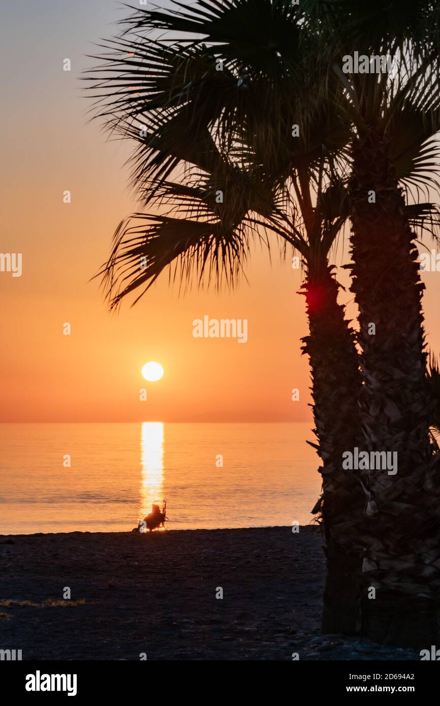 Person sitting in a hammock on the beach watching the sunset next to ...