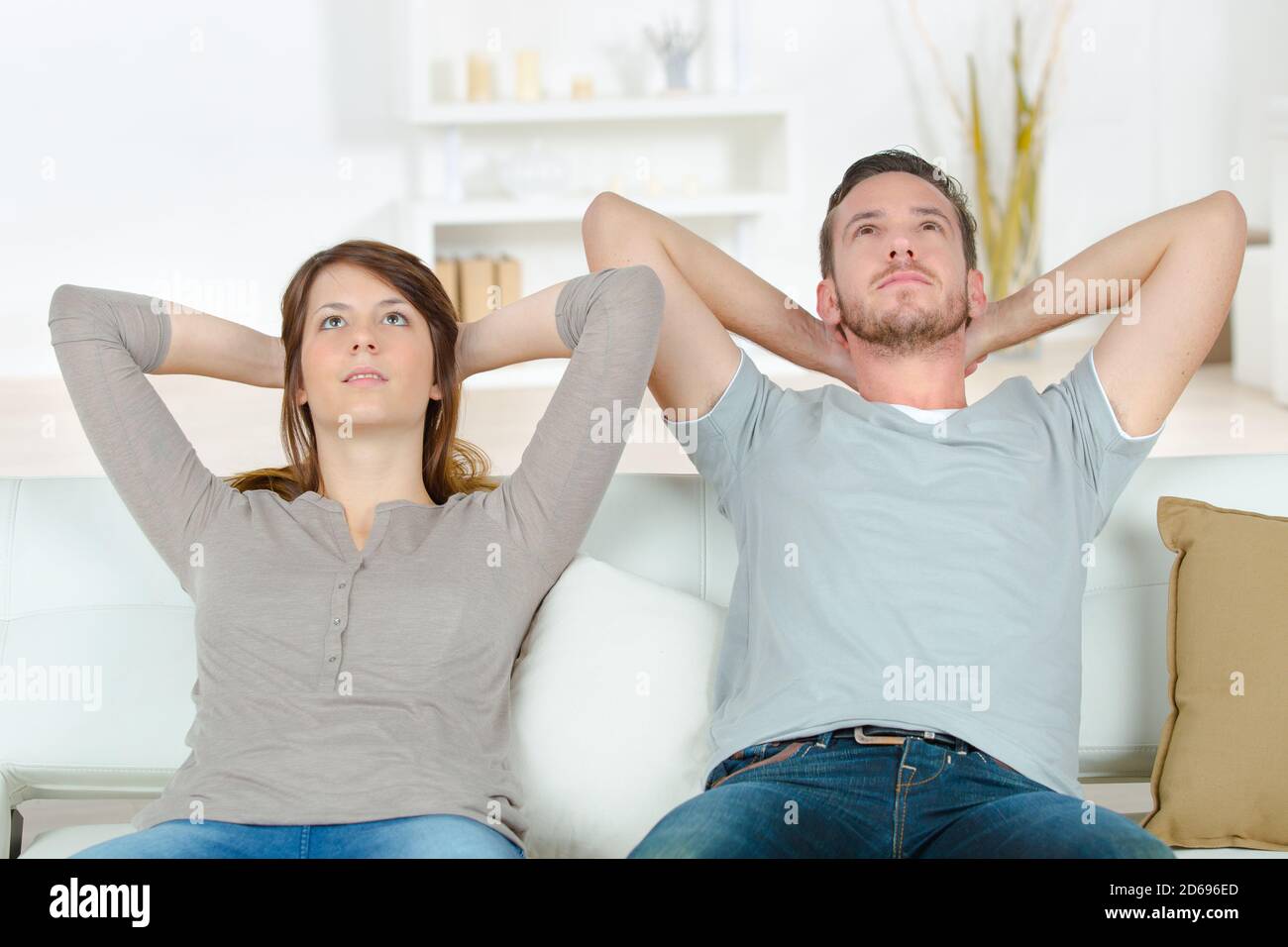 Couple on couch, arms behind their heads Stock Photo - Alamy
