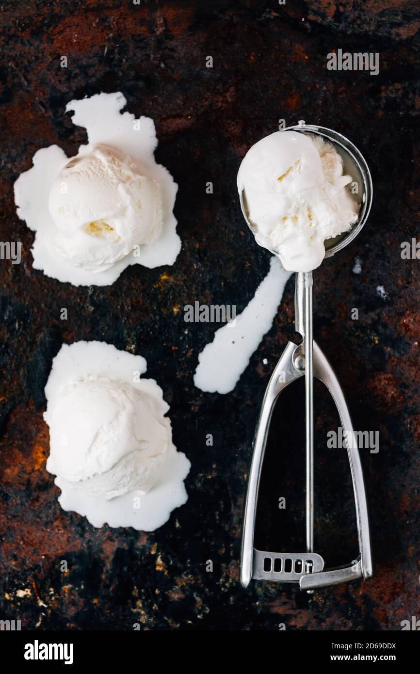 Melted ice cream in metal ice cream scooper over black rustic table ...