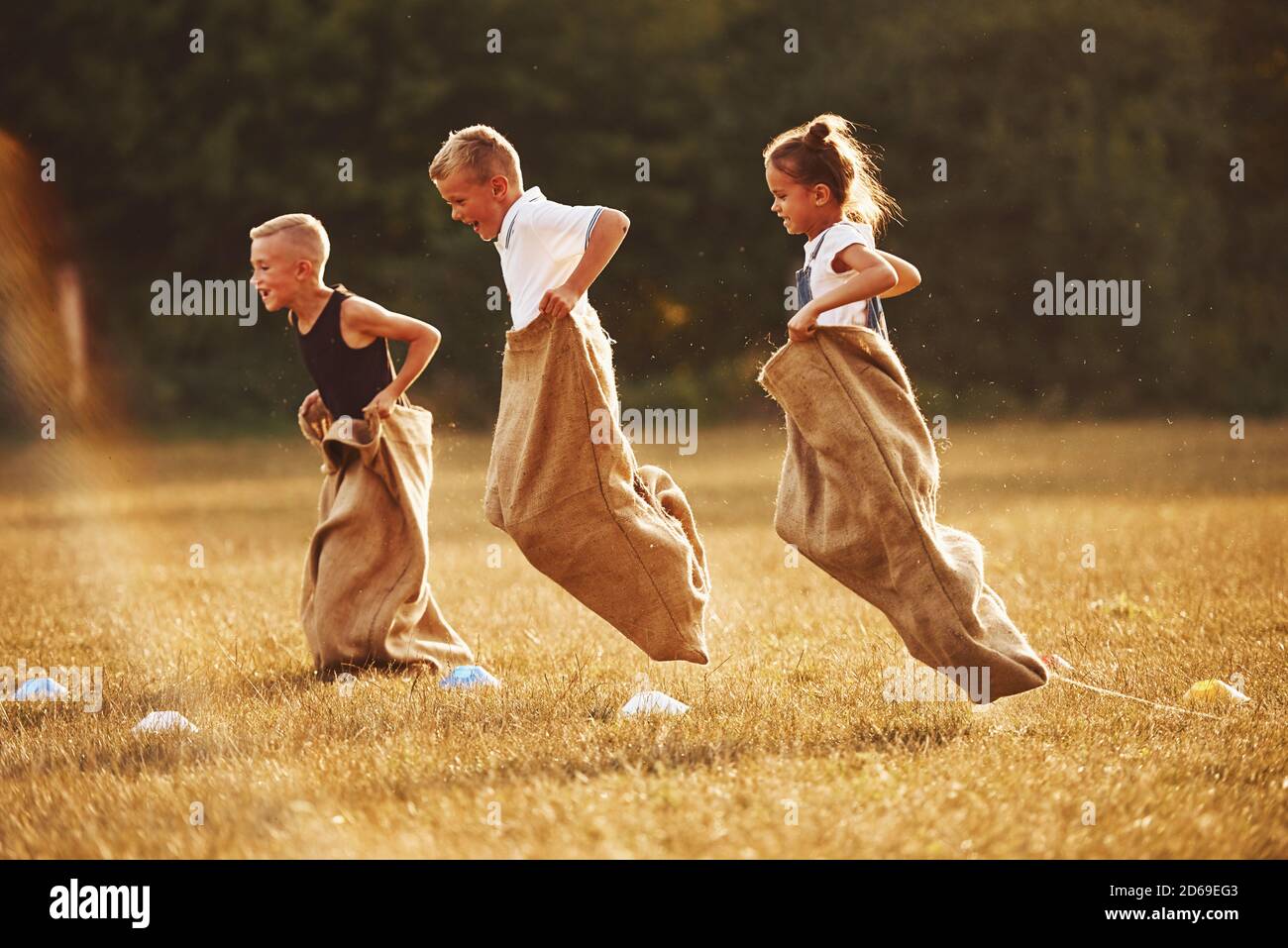 Jumping sack race outdoors in the field. Kids have fun at sunny daytime ...