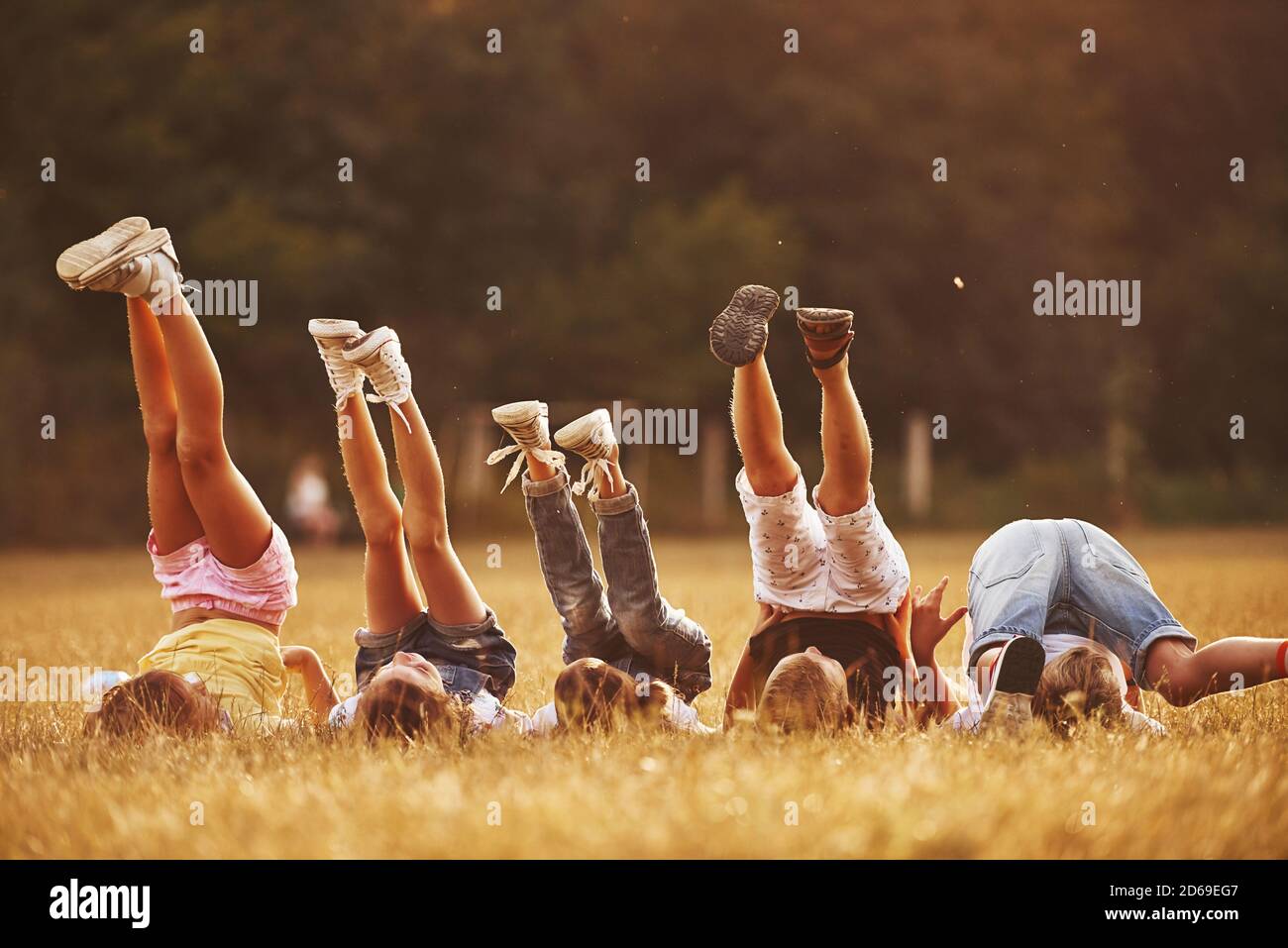 Kids resting in the field at sunny daytime together. Raising legs up ...