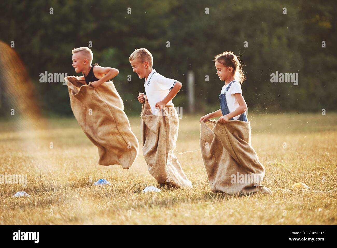 Jumping sack race outdoors in the field. Kids have fun at sunny daytime ...