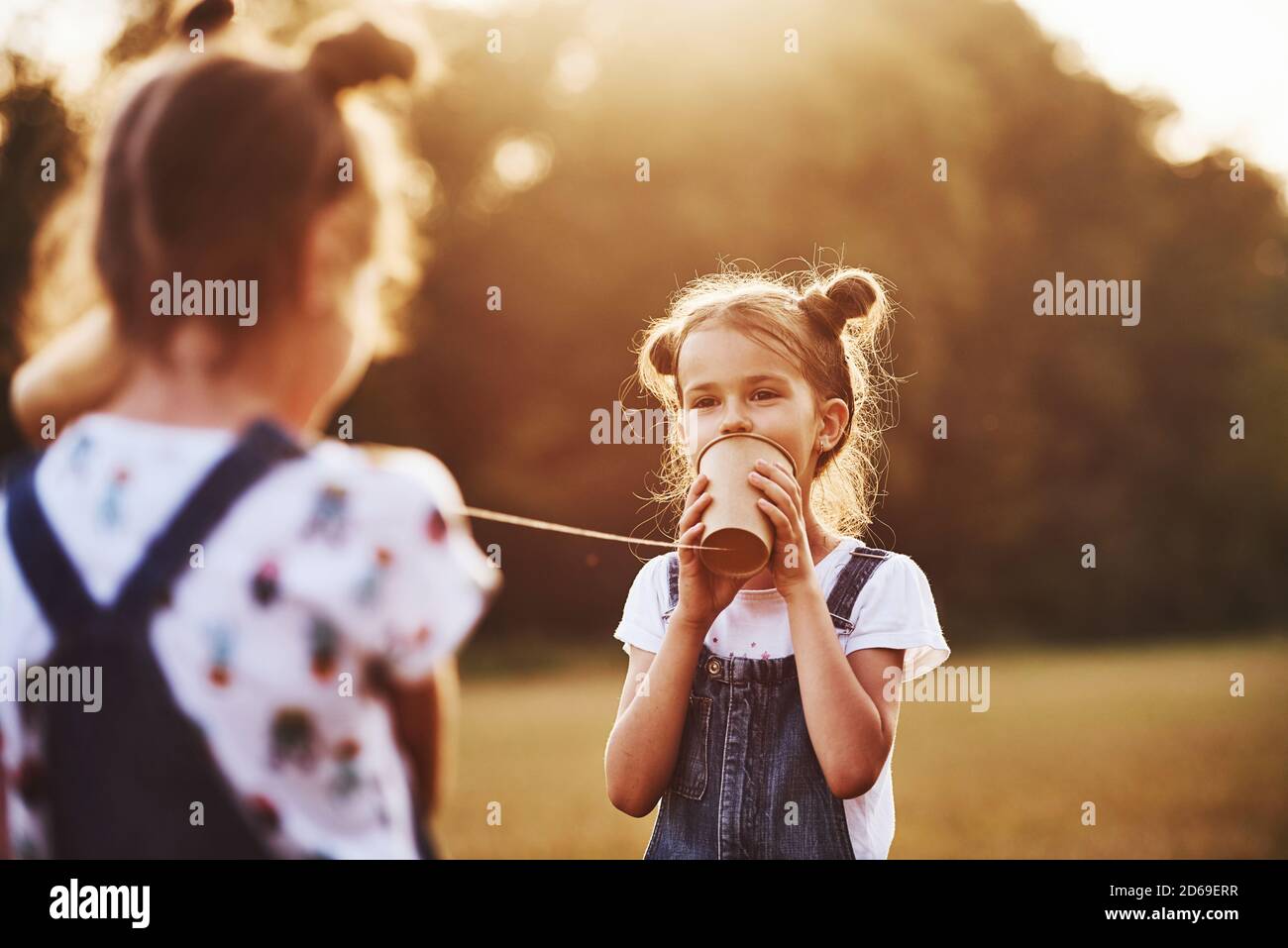 Two female kids stands in the field and talking by using string can ...