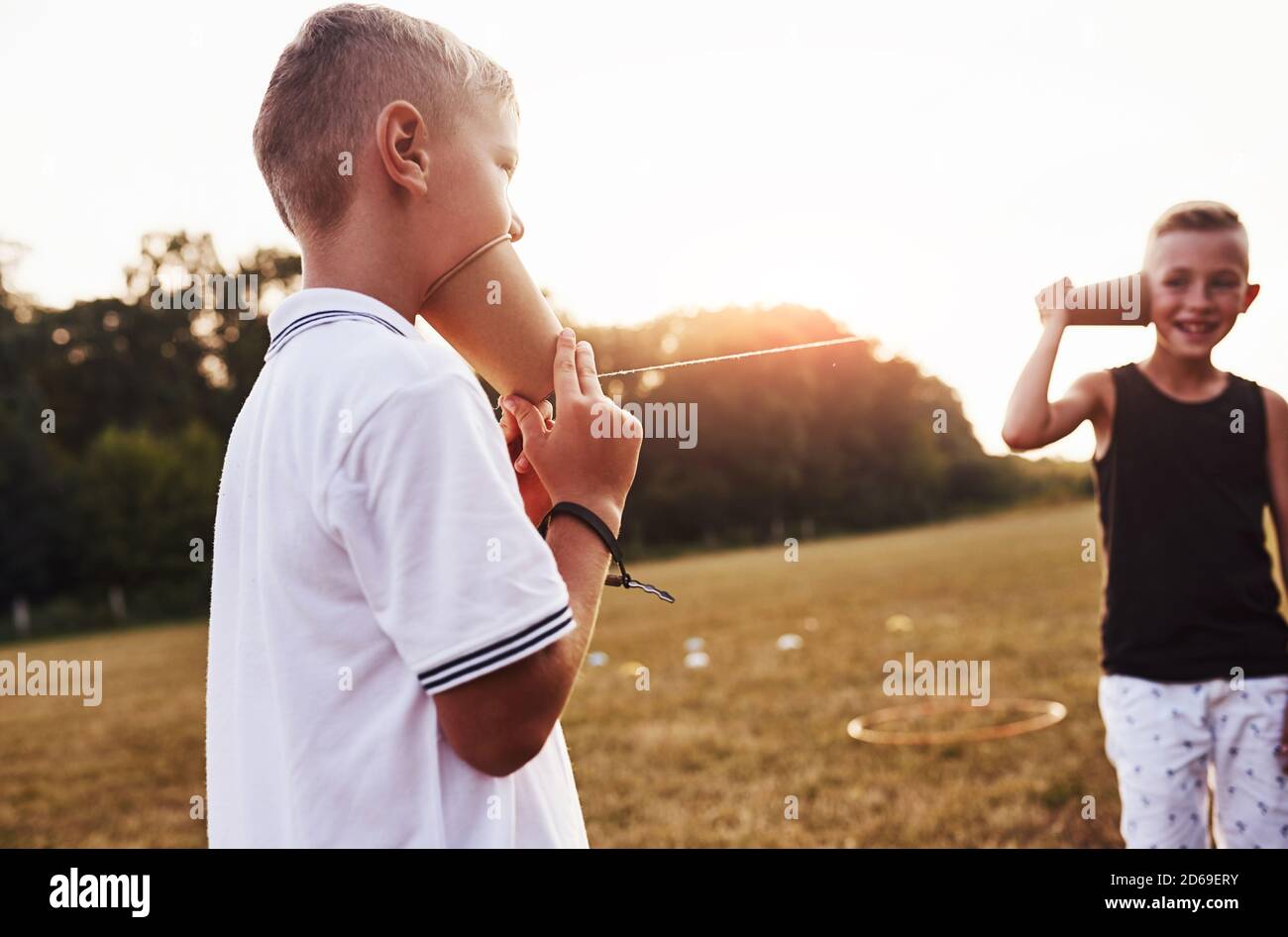 Two boys stands in the field and talking by using string can phone ...