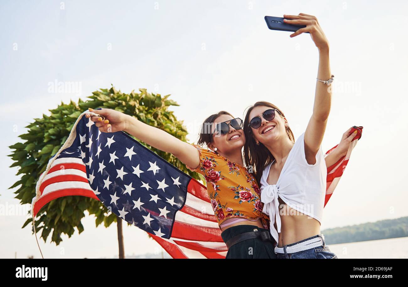 Green tree at background. Two patriotic cheerful women with USA flag in ...