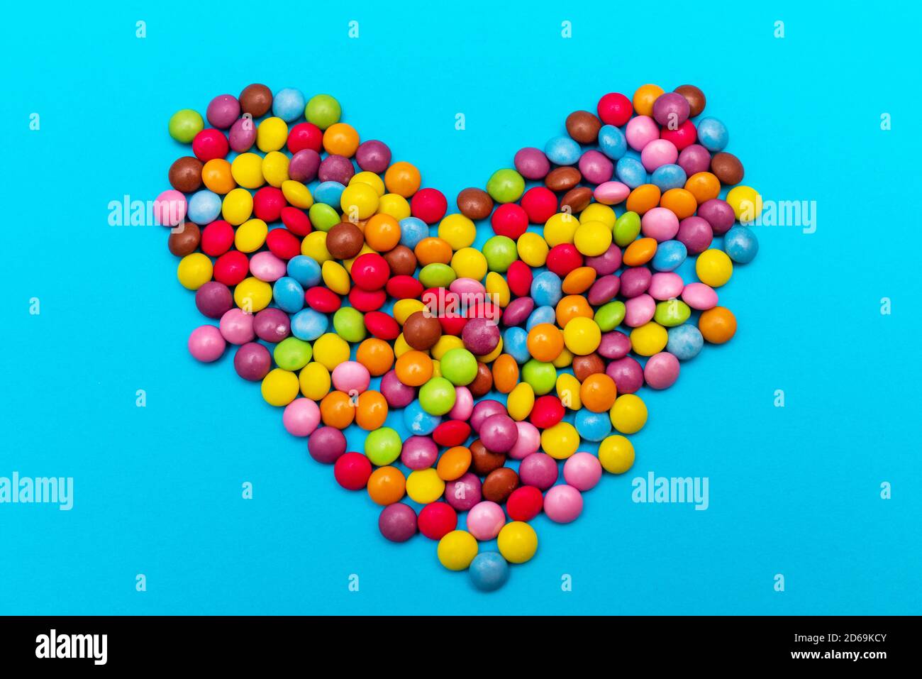 Multi-colored round candies heart shapes lie on a sparkling blue ...