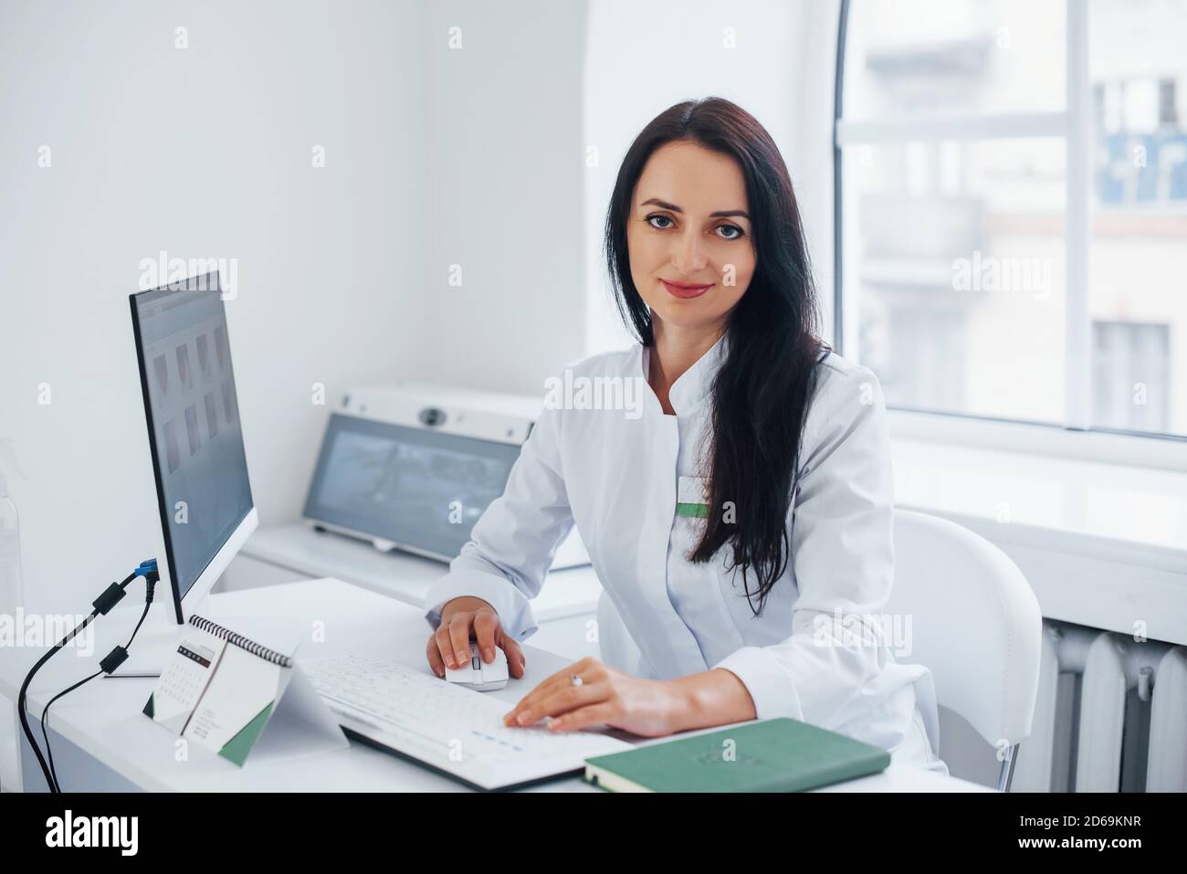 Brunette female doctor sits in modern office by computer and looks at ...