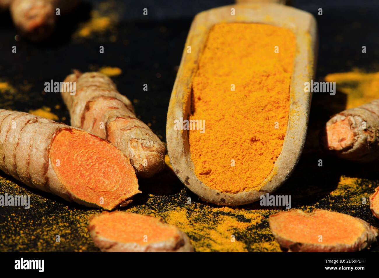 Turmeric powder (Kurkuma) in a wooden spoon and roots on a dark table ...