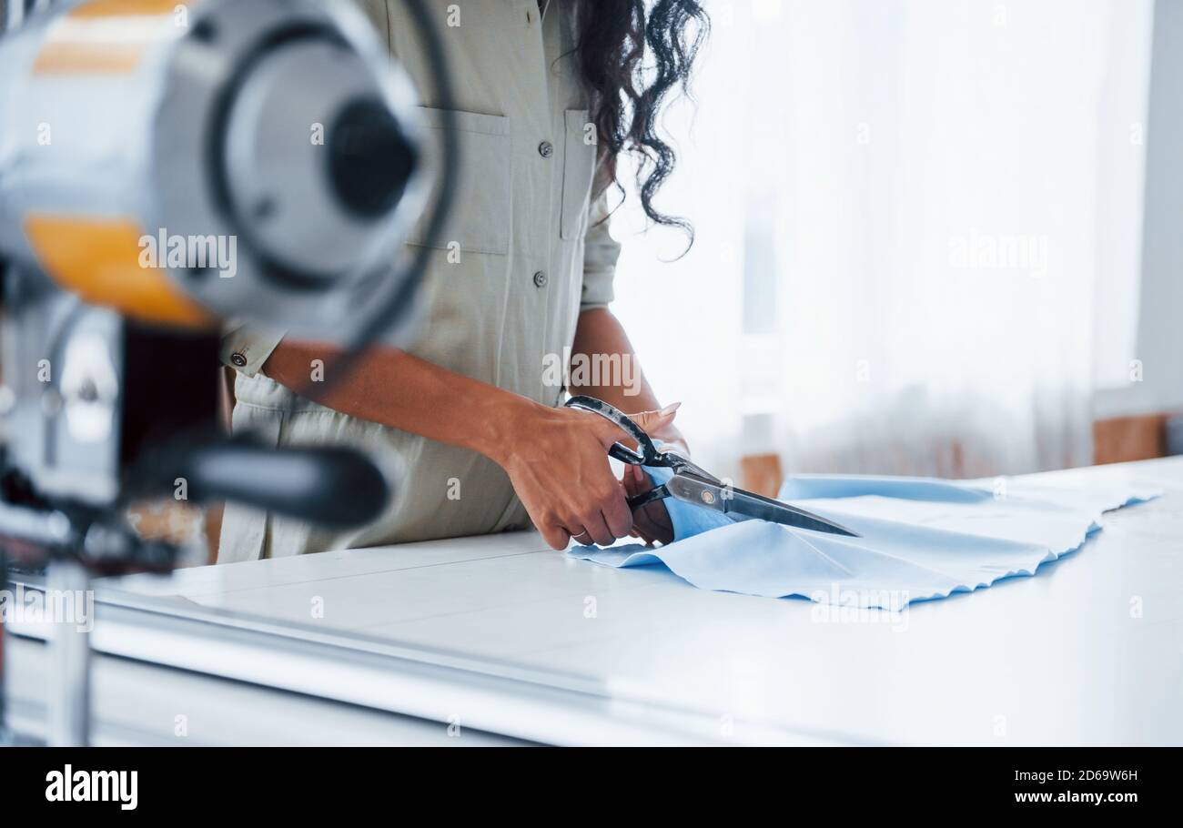 Female worker is in the sewing factory at daytime cutting cloth with ...