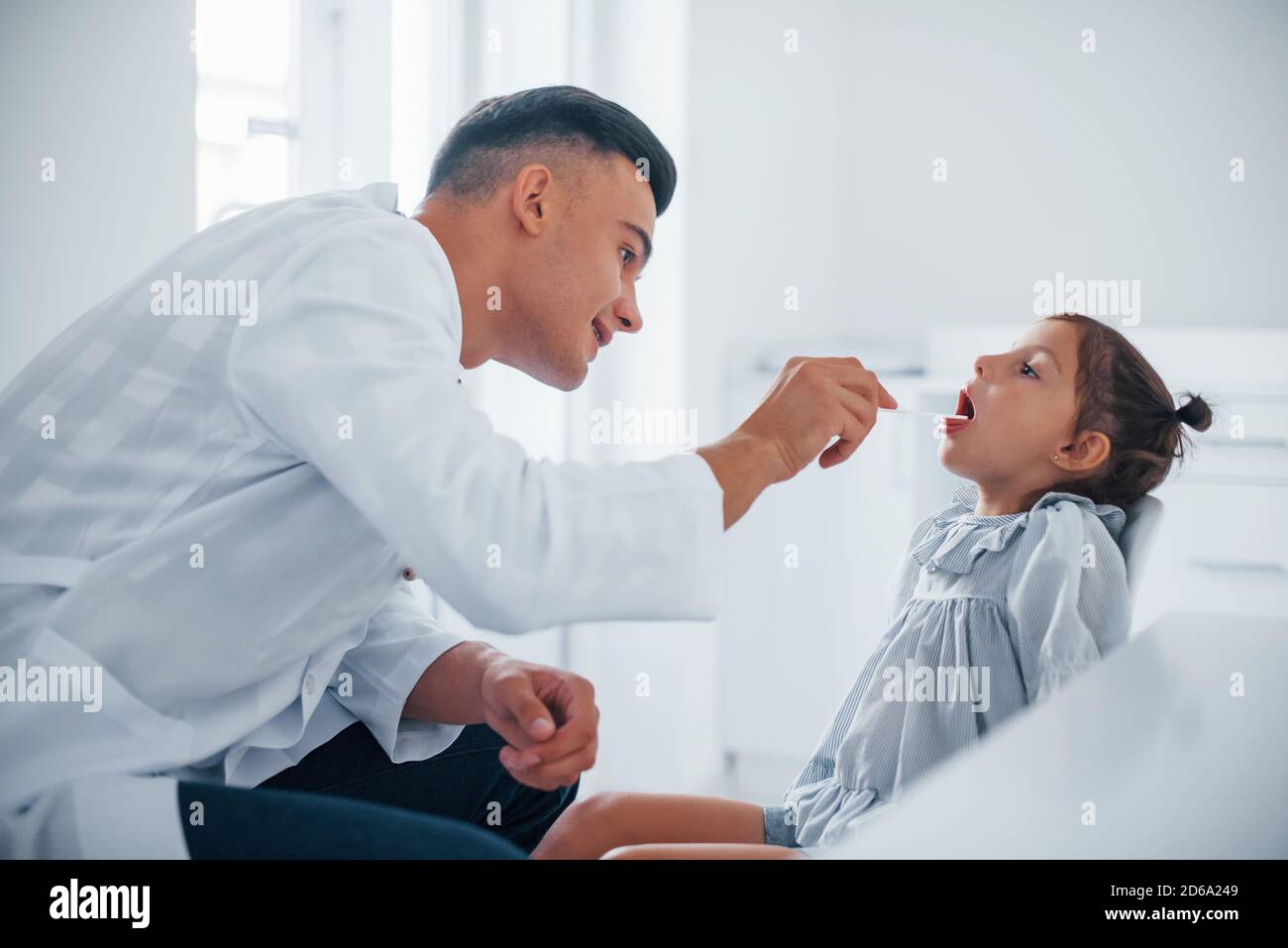 Uses tonsil to check throat. Young pediatrician works with little ...