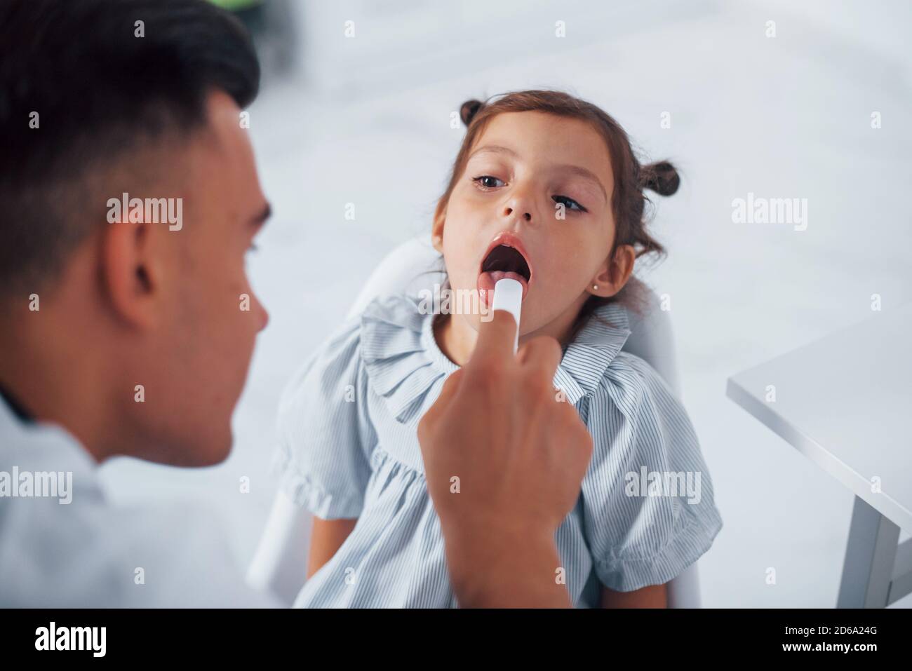 Uses tonsil to check throat. Young pediatrician works with little ...