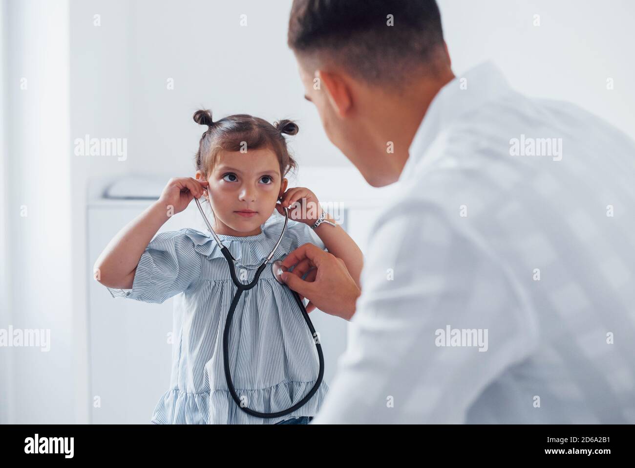 Teaches girl how to use stethoscope. Young pediatrician works with ...