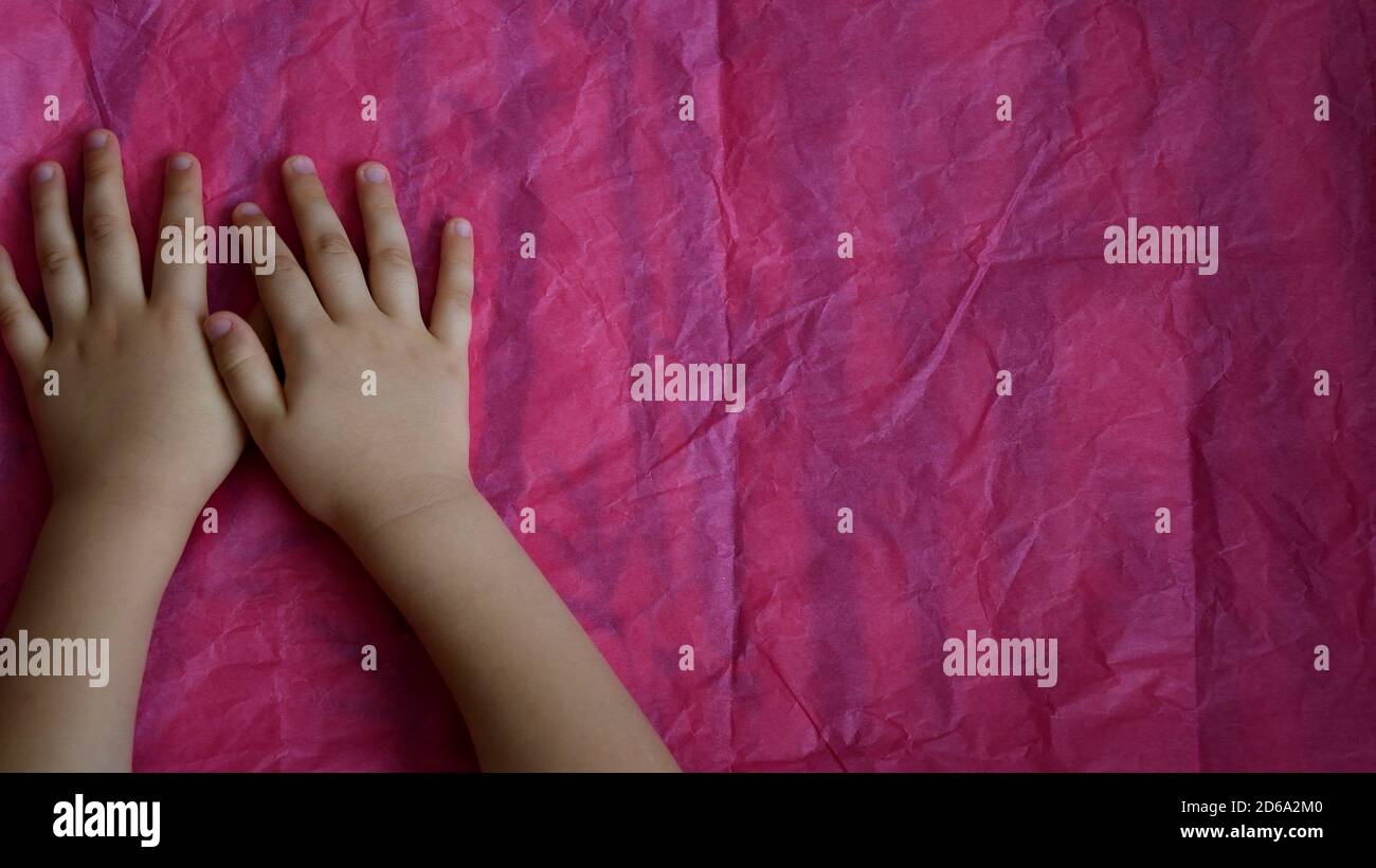 Toddler hands stop crumpled tissue paper on table. Directly above view ...